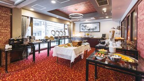 Uma sala de jantar de hotel com tapete vermelho, serviço de buffet e uma grande janela com vista para edifícios.