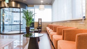 Um hall com uma recepção em curva, um vaso de planta, uma estante de livros e uma fileira de cadeiras laranja.
