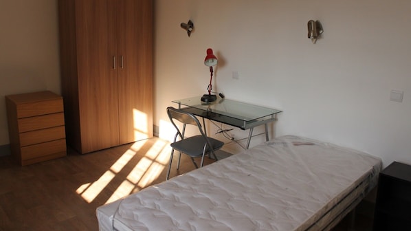 Um quarto com cama, escrivaninha, cadeira, guarda-roupa e abajur.