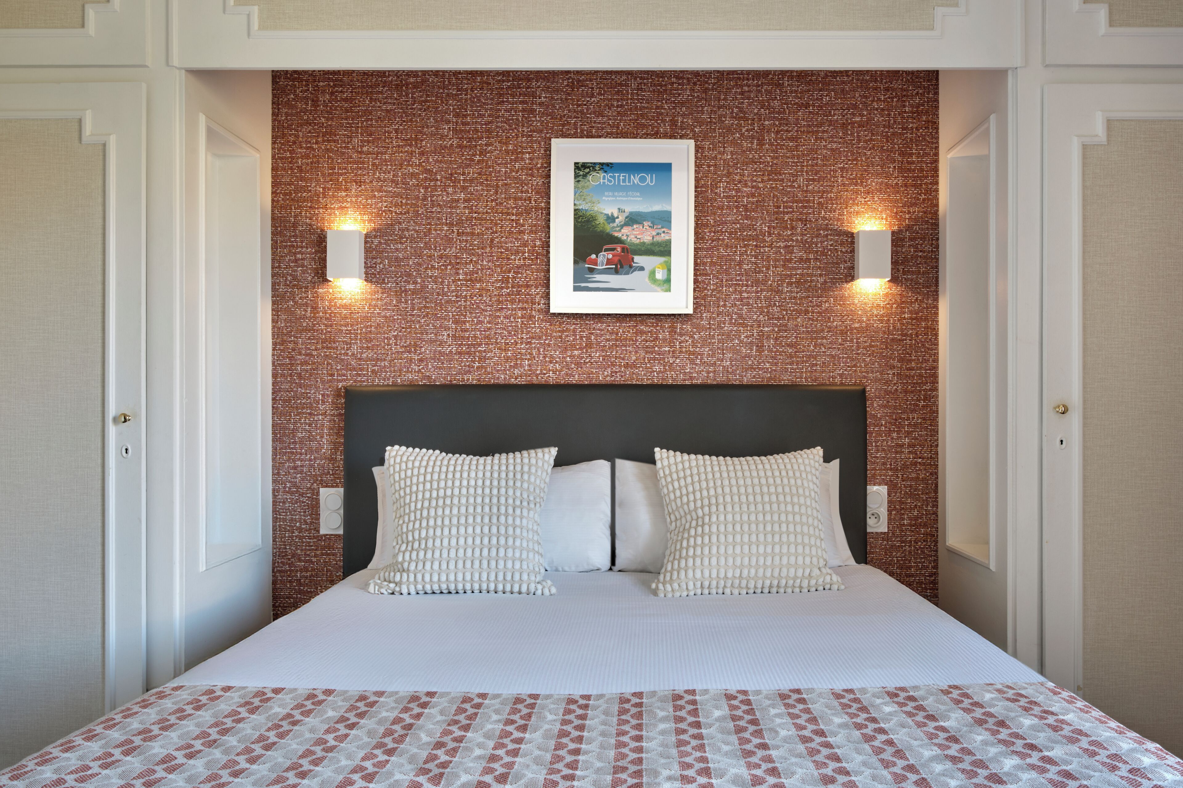 Cama bem arrumada com colcha estampada, parede com padrão de tijolos e duas luminárias fixadas na parede.