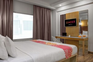 Quarto de hotel com cama, escrivaninha, laptop e um letreiro que diz "GINGER An IHC Hotels Brand".