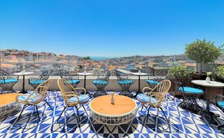 Terraço com cadeiras e mesas de vime, com vista para um horizonte urbano repleto de edifícios e céu claro.