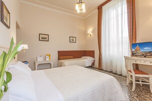 Quarto de hotel com uma cama grande, uma escrivaninha com cadeira, uma televisão e uma janela com cortinas.