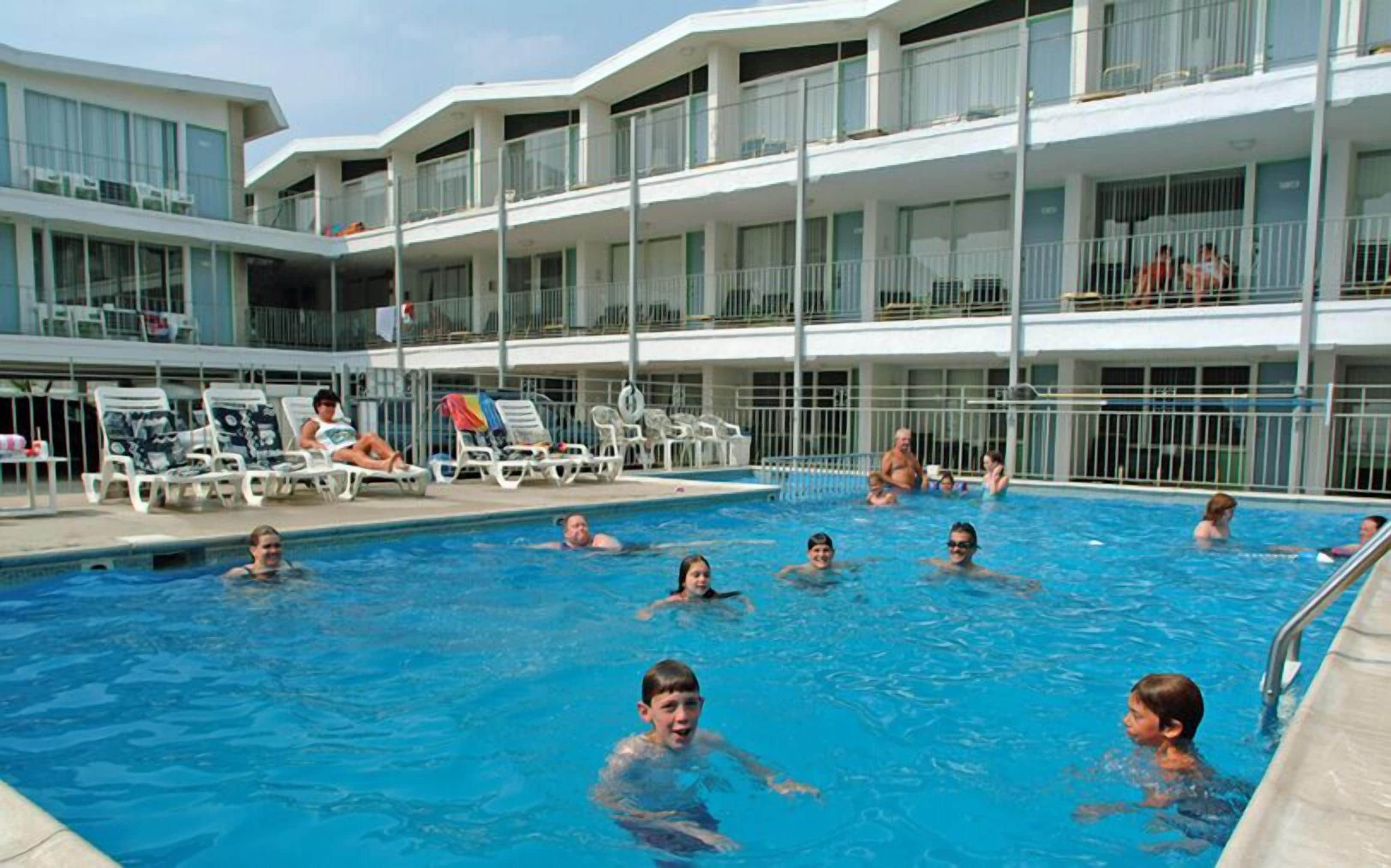 Área de piscina com vários níveis de varandas, espreguiçadeiras e um céu azul límpido.