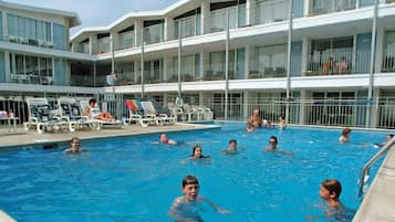 Área de piscina com vários níveis de varandas, espreguiçadeiras e um céu azul límpido.