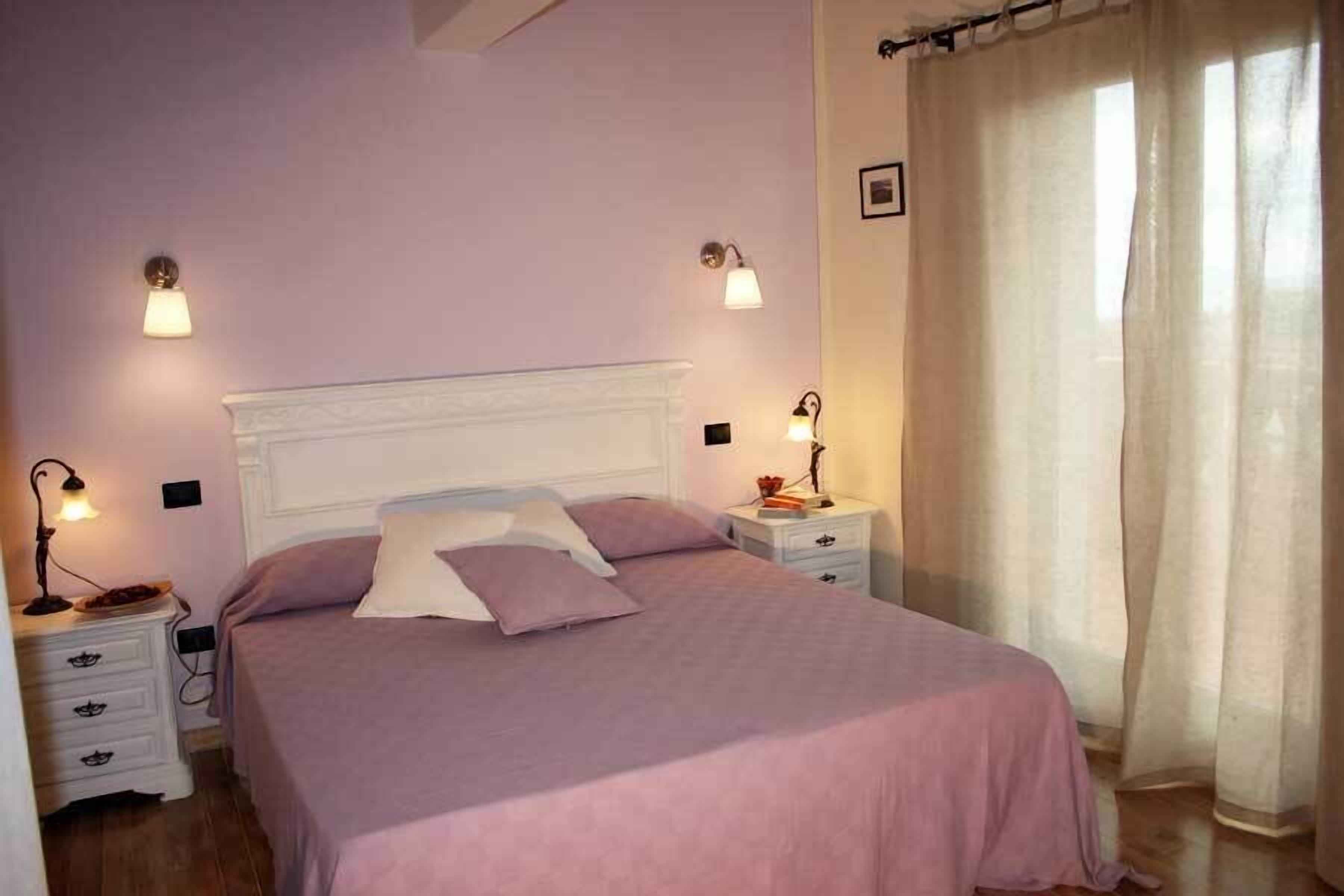 Quarto com cama, mesas de cabeceira e luminárias de parede.