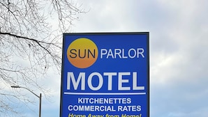 Placa de motel com o nome 'Sun Parlor Motel' e menções a cozinhas equipadas, tarifas comerciais e a mensagem 'Feliz Natal'.