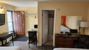 Quarto de hotel com duas camas, uma escrivaninha com cadeira, televisão, banheiro visível por uma porta aberta e um aviso de proibido fumar na parede.