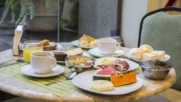 Uma mesa de café da manhã com diversos alimentos, xícaras e uma colher.