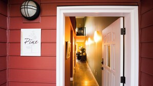 Um corredor com uma placa indicando "Pine", uma luminária na parede e uma porta que dá para um quarto com varanda.
