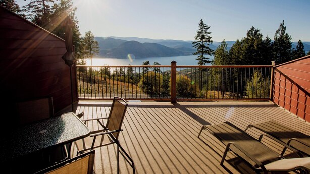Um deck de madeira com uma mesa e cadeiras, com vista para um lago e montanhas.