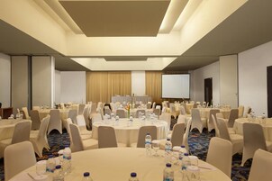 Sala de conferências com mesas redondas, cadeiras e uma tela de projeção.