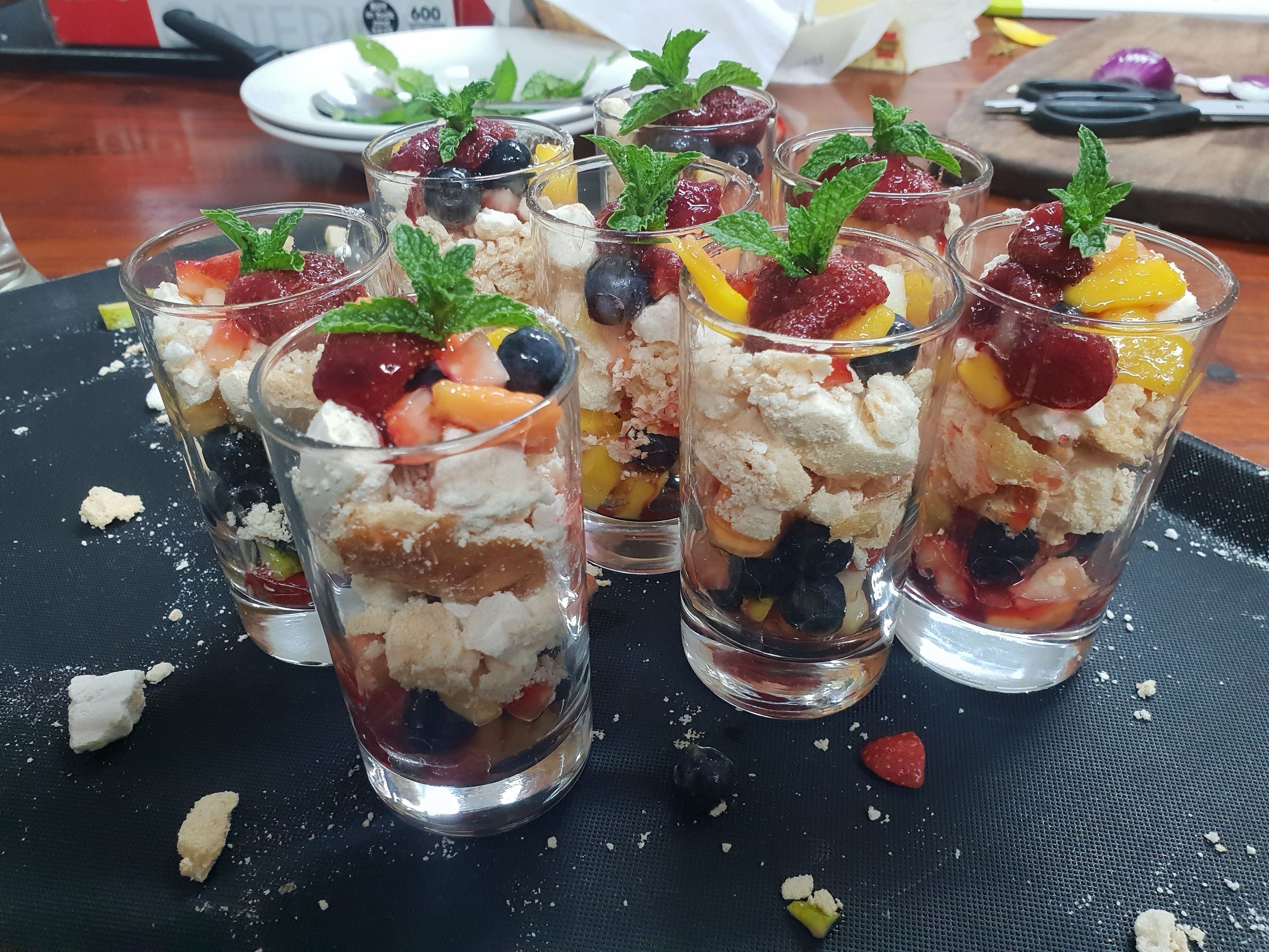 Uma bandeja com copinhos de sobremesa, fruta e creme, sobre um tapete preto.