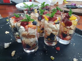 Uma bandeja com copinhos de sobremesa, fruta e creme, sobre um tapete preto.