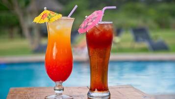 Duas bebidas com guarda-chuvas sobre uma mesa de madeira junto a uma piscina.