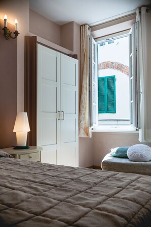Quarto com cama, mesa de cabeceira com luminária, guarda-roupa e janela com cortinas.