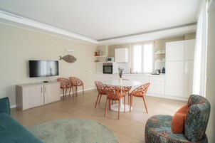 Uma sala de estar moderna com televisão, sofá e zona de refeições com cadeiras e mesa.