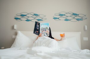 Uma pessoa deitada na cama lendo um livro chamado 'Grand Stories', com um copo de suco de laranja.