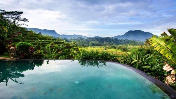 Visão nítida de uma piscina com o reflexo da vegetação exuberante ao redor e montanhas distantes.