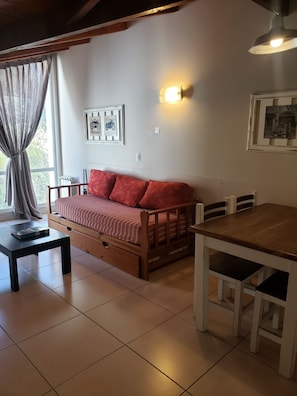 Um quarto acolhedor com um sofá de madeira, uma mesinha, uma mesa de jantar e uma janela com cortinas.