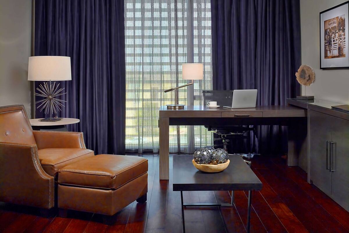 Quarto de hotel moderno com sofá de couro, escrivaninha com laptop, xícara de café e uma tigela decorativa.