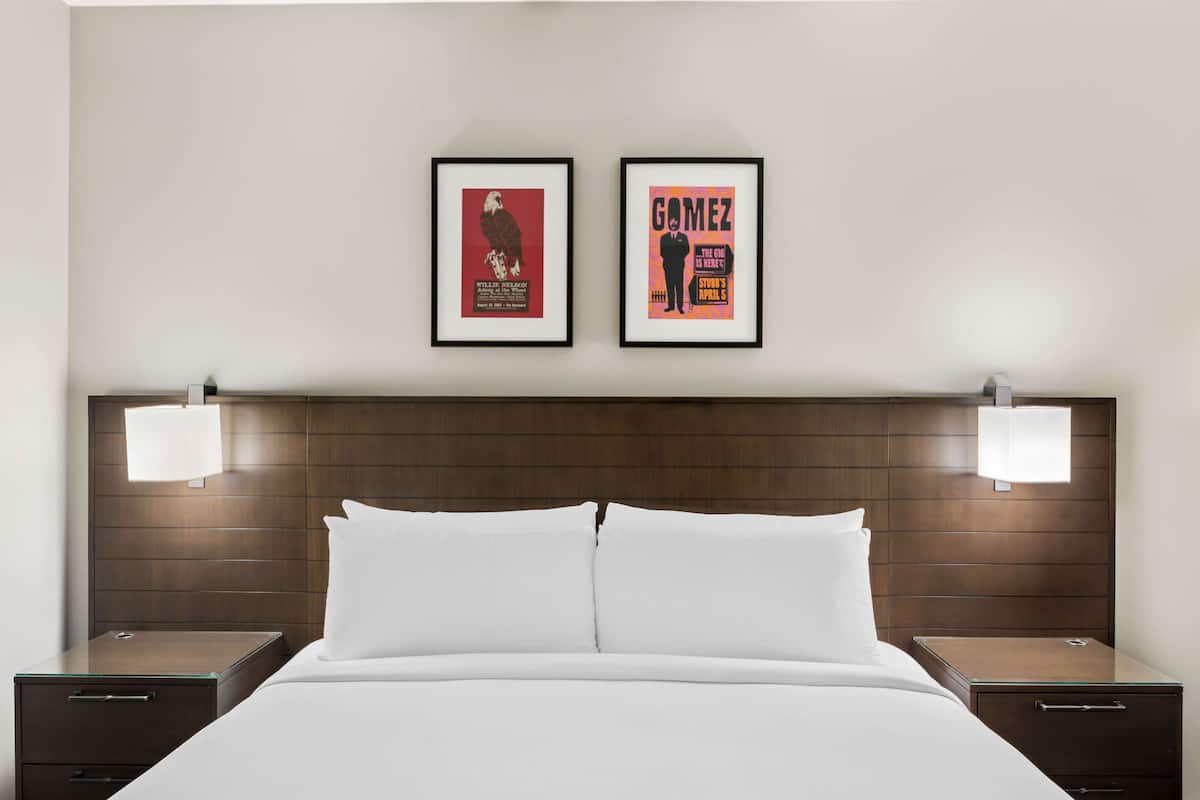 Quarto de hotel com uma cama grande, duas mesas de cabeceira e dois quadros emoldurados na parede.