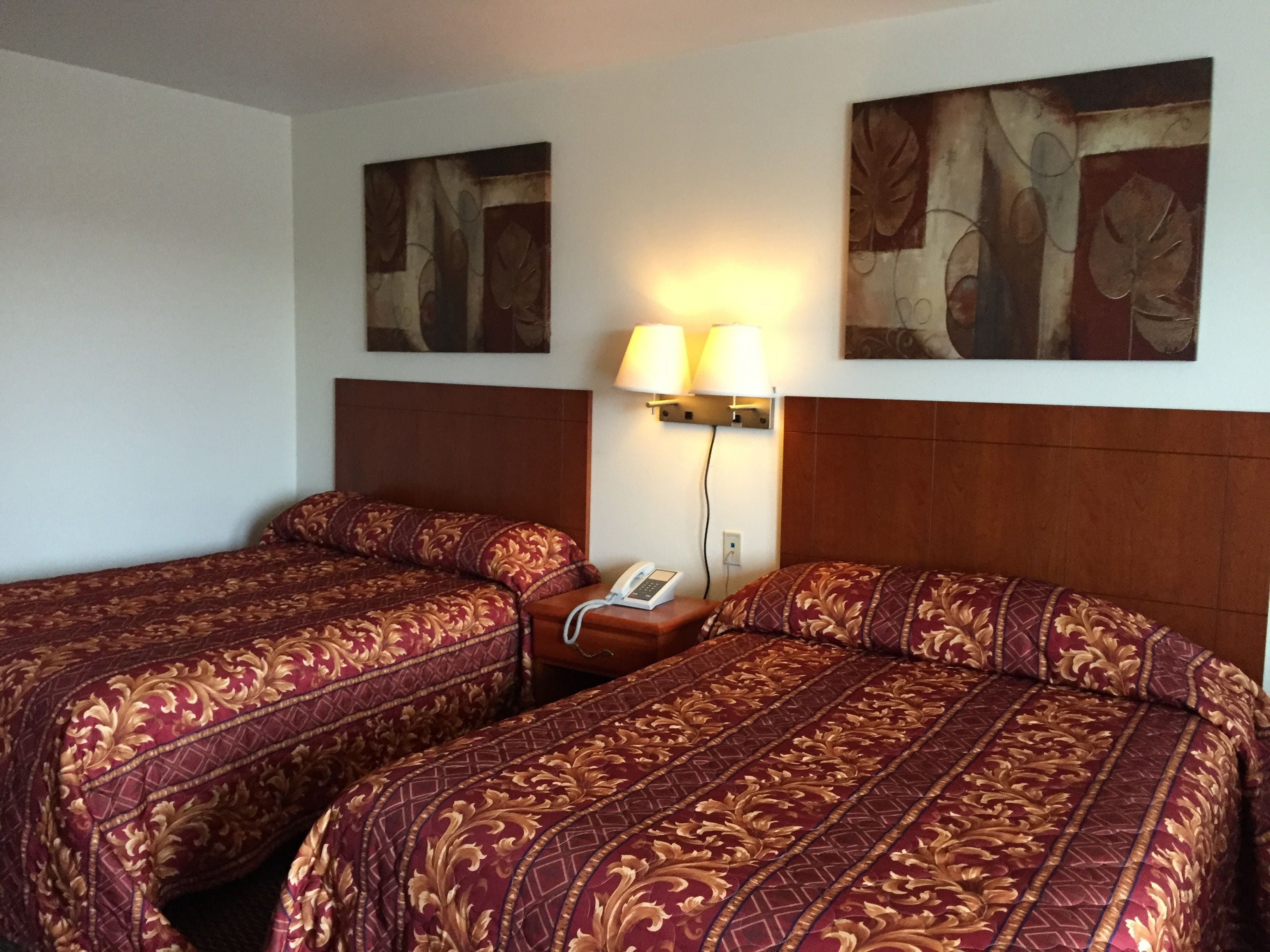 Quarto de hotel com duas camas, uma mesa de cabeceira com telefone e luminárias fixadas na parede.