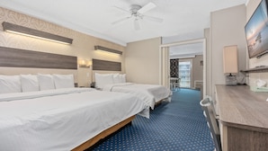 Quarto de hotel com duas camas, uma escrivaninha, televisão e ventoinha no teto.