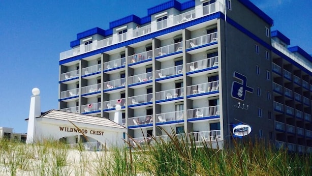 Um hotel com vários andares, varandas, placa de guarda-sol de praia e um primeiro plano arenoso.