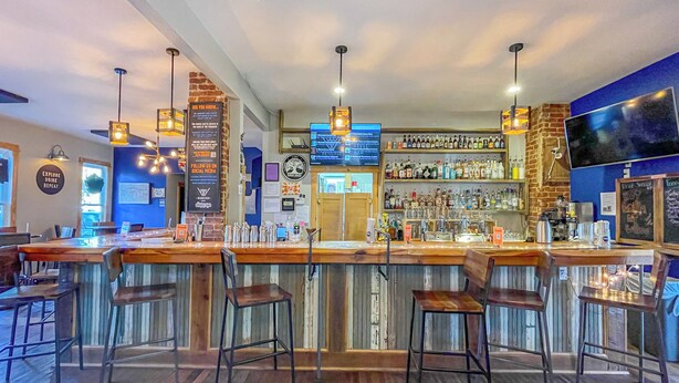 Um bar com banquetas de madeira, um balcão e diversas garrafas.