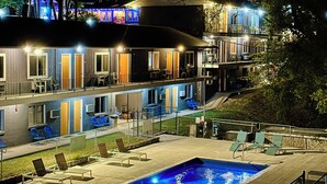 Um edifício de dois andares com piscina, área de estar externa e fachada bem iluminada.