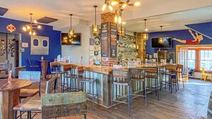 Um bar com vários bancos e um balcão, uma televisão presa na parede, e uma parede de tijolos com diversos sinais e decorações.