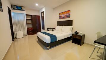 Quarto de hotel com cama, mesa de cabeceira, escrivaninha, cadeira, guarda-roupa e um quadro na parede.