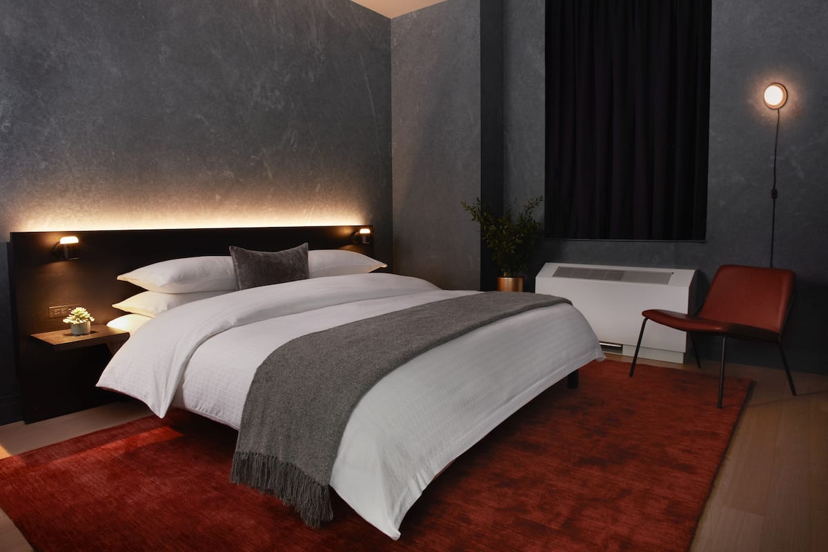 Quarto moderno com uma cama grande, luminárias de cabeceira, um tapete vermelho e uma cadeira.