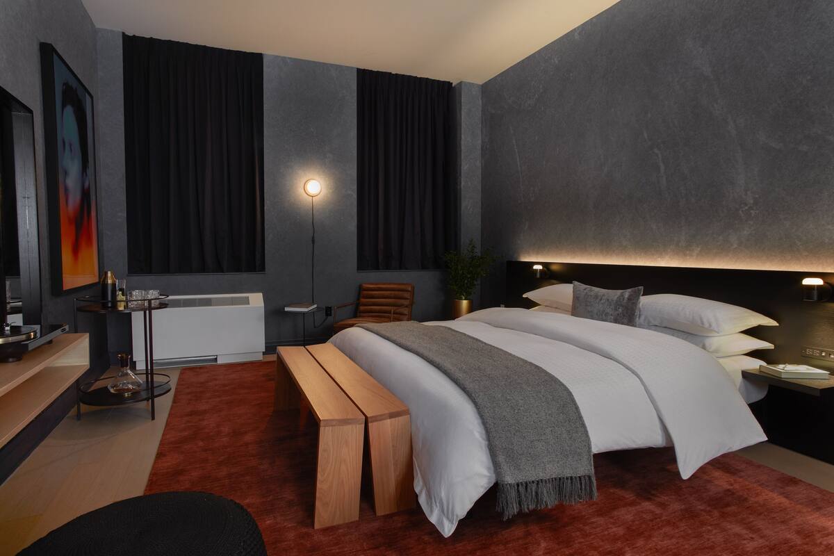 Quarto moderno com uma cama grande, mesas de cabeceira, um banco, uma escrivaninha e uma janela com cortinas.