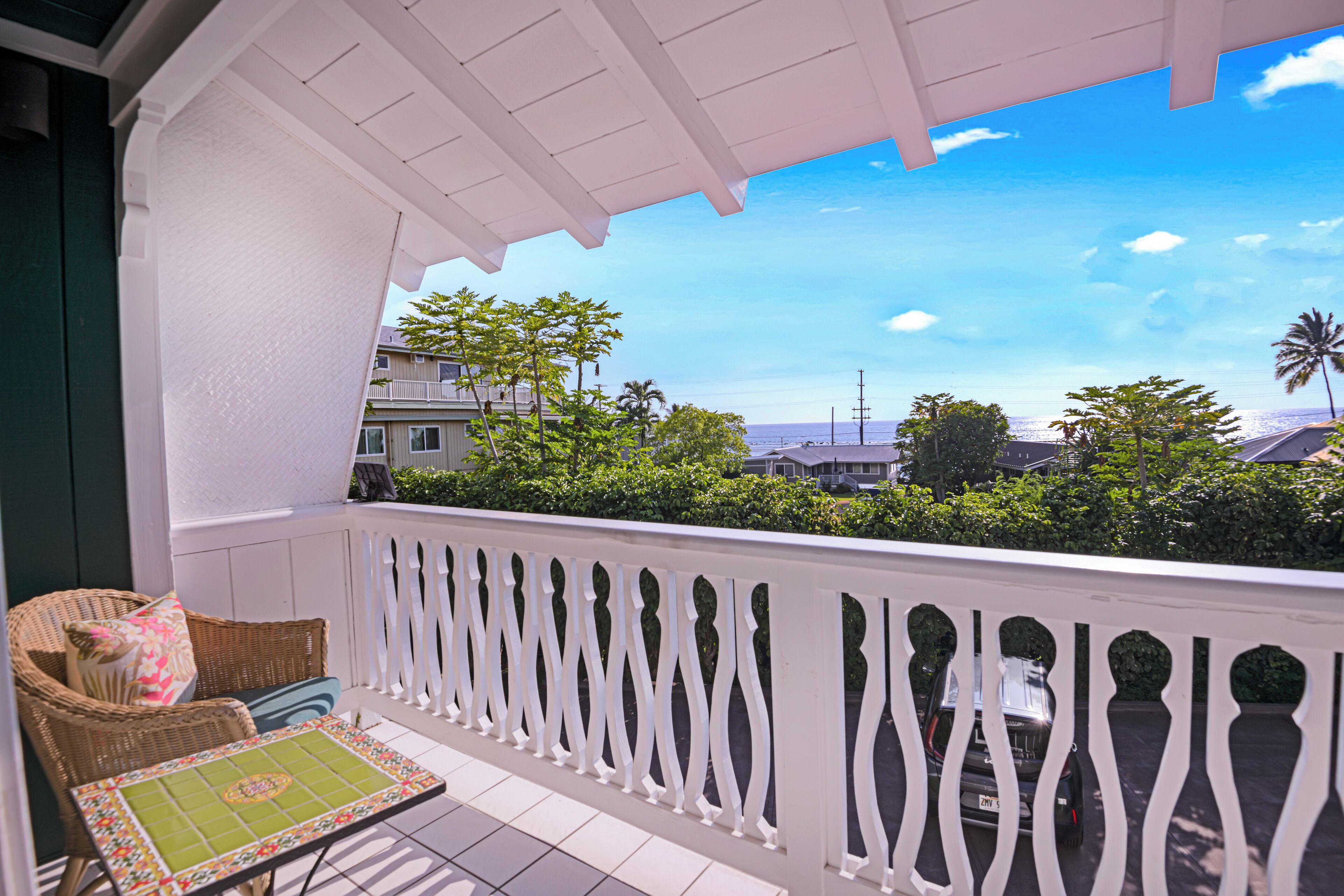 Uma varanda com guarda-corpo branco, móveis de vime e vista para o mar e casas vizinhas.