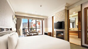 Quarto de hotel com uma cama grande, televisão, lareira e varanda com vista para montanhas.
