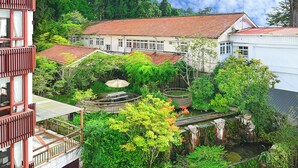 Área residencial com uma casa de telhado vermelho, cercada por vegetação exuberante e um pequeno lago.