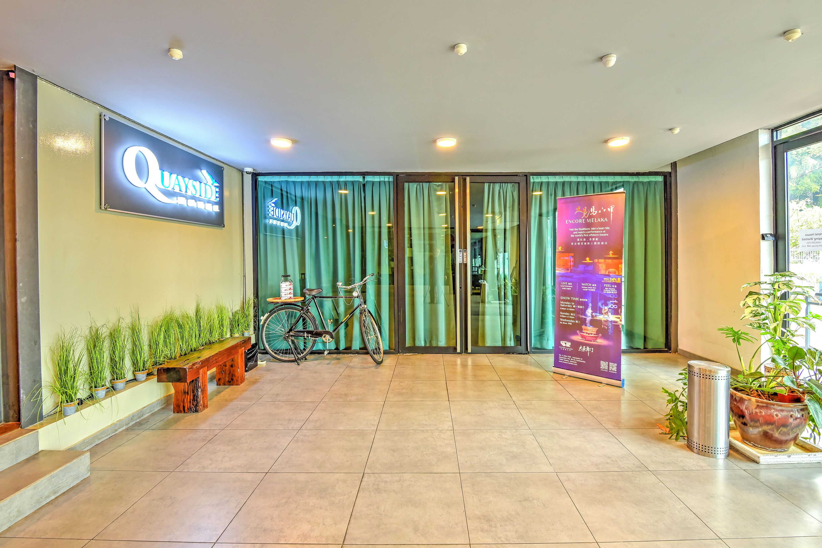 Entrada de hotel com placa, bicicleta, banco e planta em vaso.