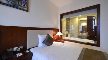 Quarto de hotel com uma cama grande, uma mesa de cabeceira com abajur, telefone e um quadro na parede.