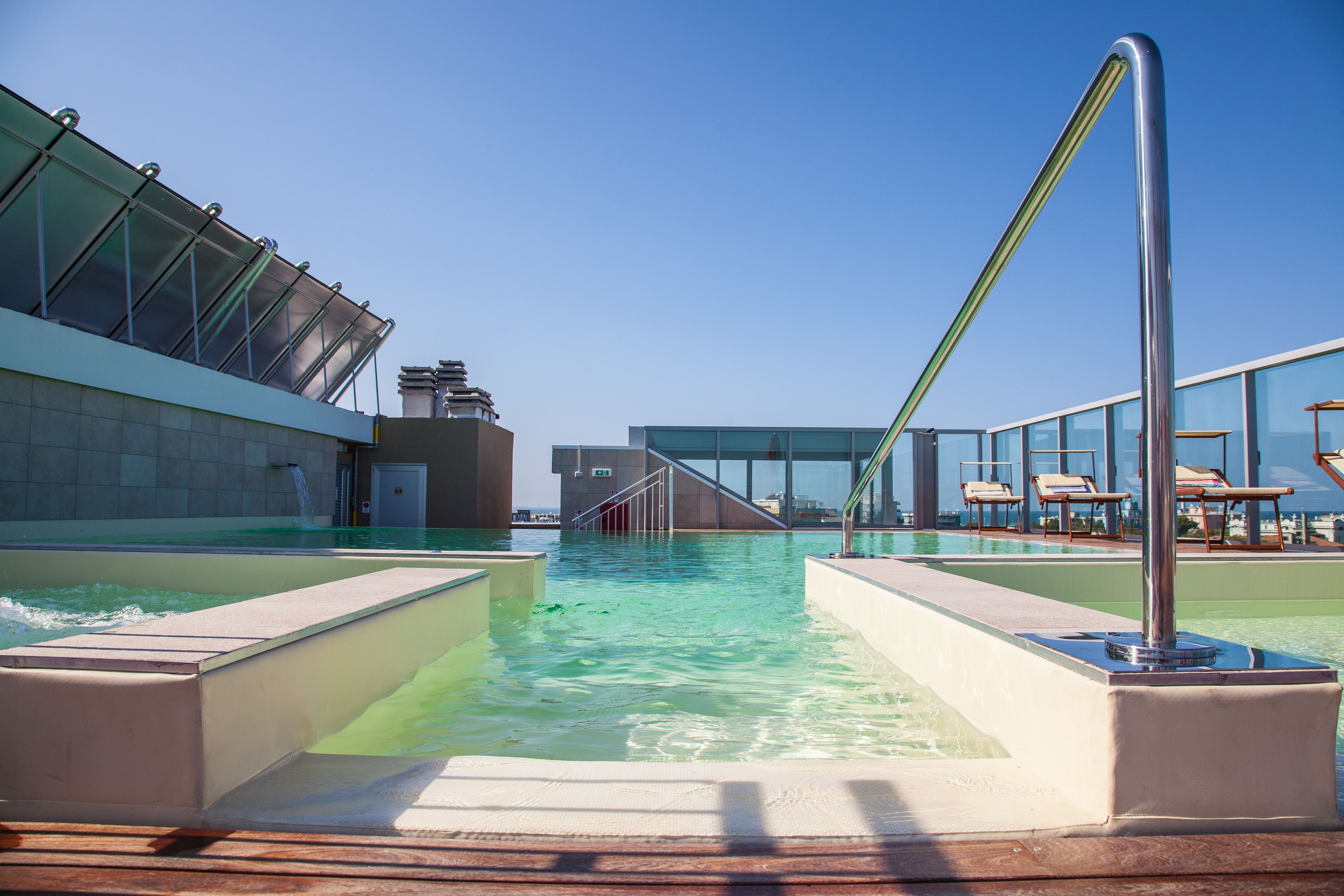 Área de piscina com água cristalina, estrutura metálica e espreguiçadeiras.