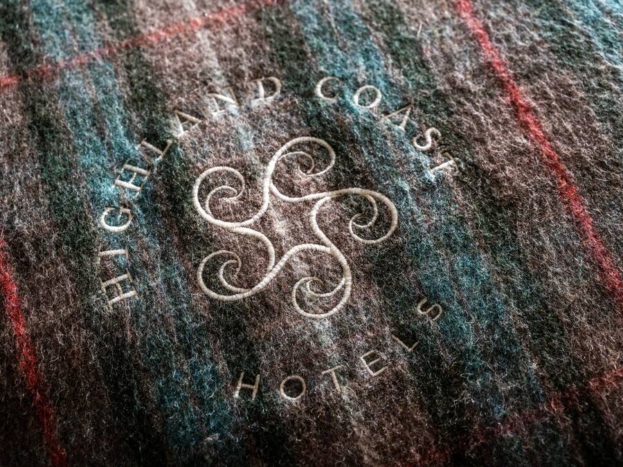 Tecido texturizado com bordado que diz 'HIGHLAND COAST HOTELS'.