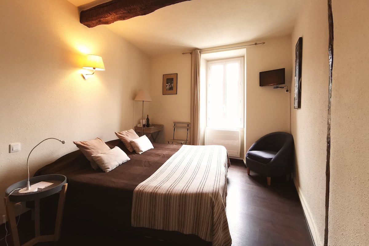 Quarto de hotel com cama, luminária de cabeceira, cadeira e televisão na parede.