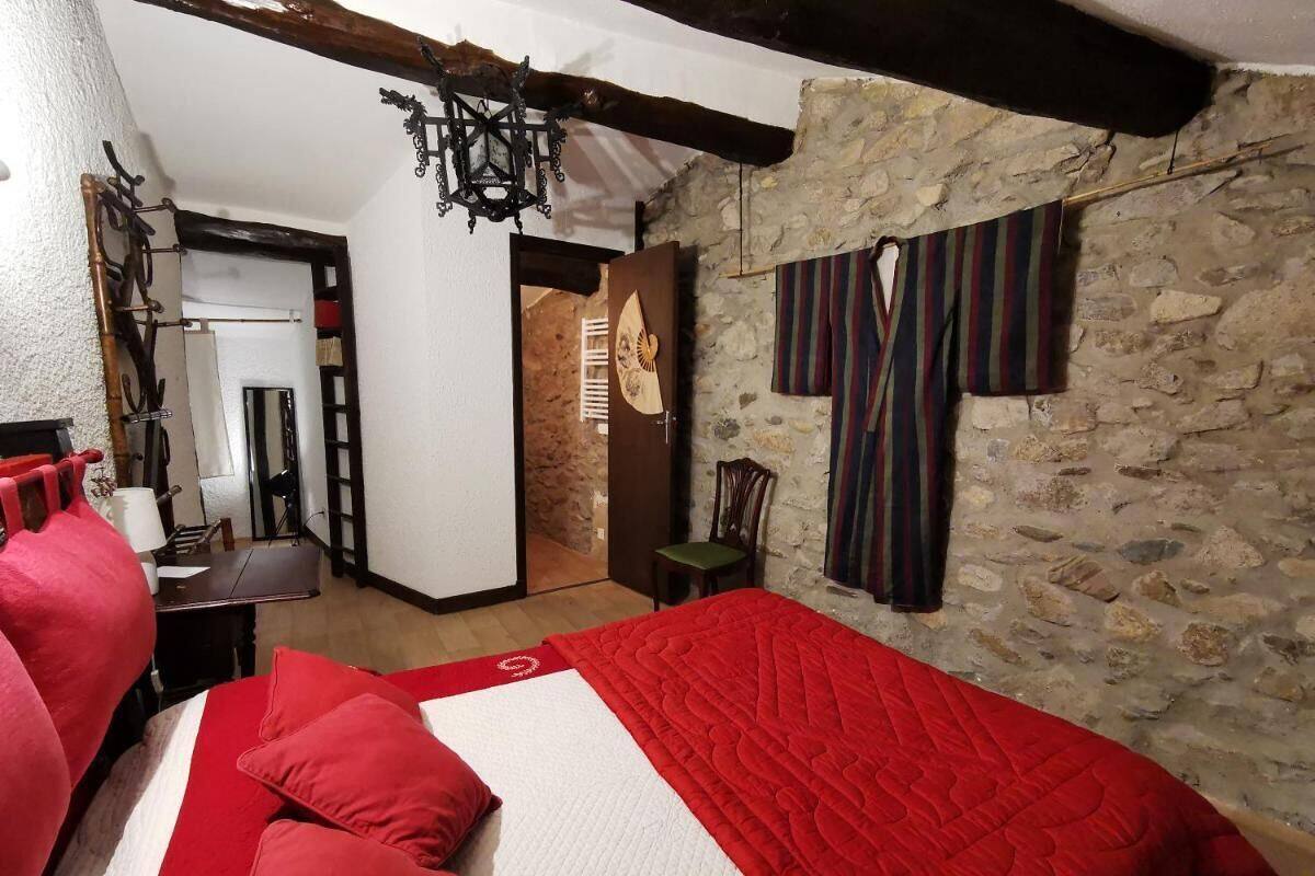 Um quarto com uma cama, uma cadeira, uma mesa e uma parede de pedra.