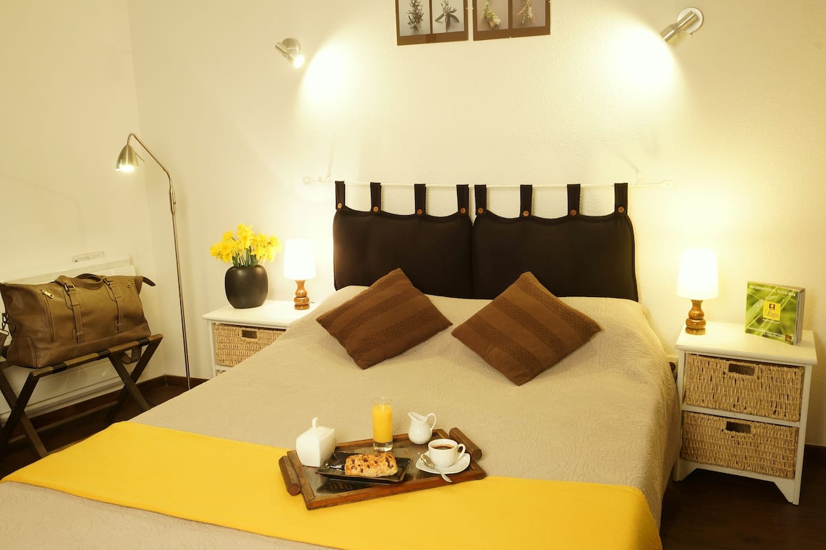 Cama arrumada com uma bandeja de café da manhã, uma luminária e um porta-retrato na mesinha de cabeceira.