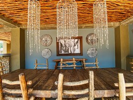 Uma zona de refeições rústica com uma mesa de madeira e bancos, rodeada por adornos nas paredes e um candeeiro pendente.