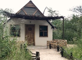 Uma casa pequena e rústica com entrada em parede de pedra, porta de madeira e uma janela.