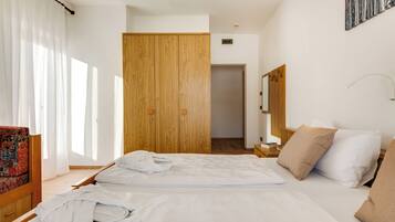 Quarto de hotel com cama, guarda-roupa de madeira, espelho e janela com cortinas.