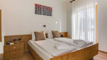 Uma cama bem arrumada com lençóis brancos, cabeceira de madeira e mesa de cabeceira com uma luminária.