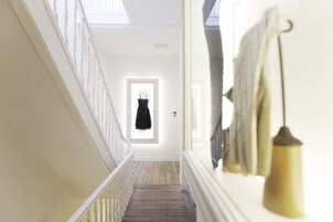 Uma escadaria com corrimãos brancos que leva a um quarto com um quadro emoldurado e um candeeiro suspenso.